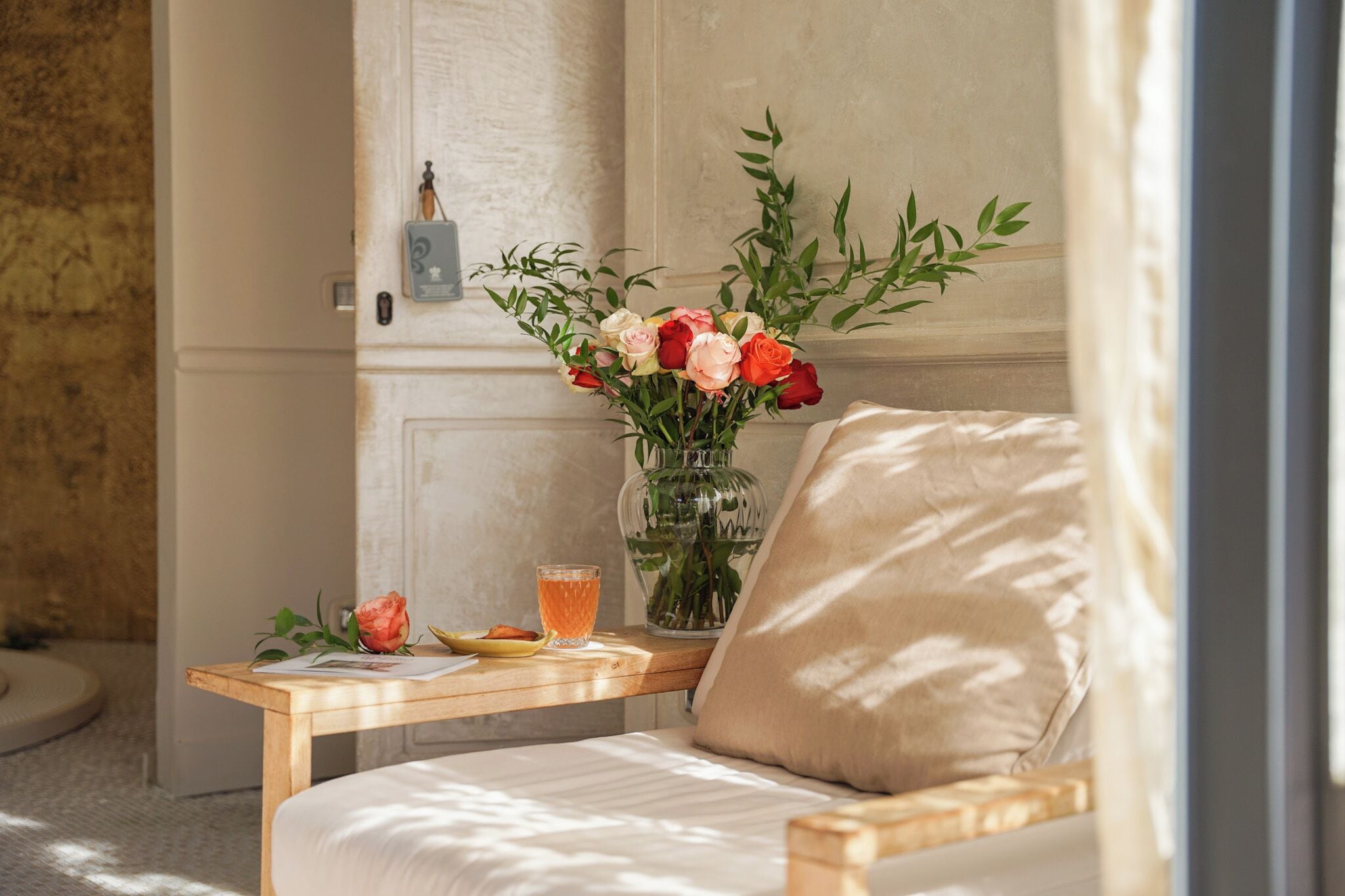 Um quarto aconchegante com uma mesa de madeira, um vaso de flores, um copo de bebida de laranja e um sofá bege.