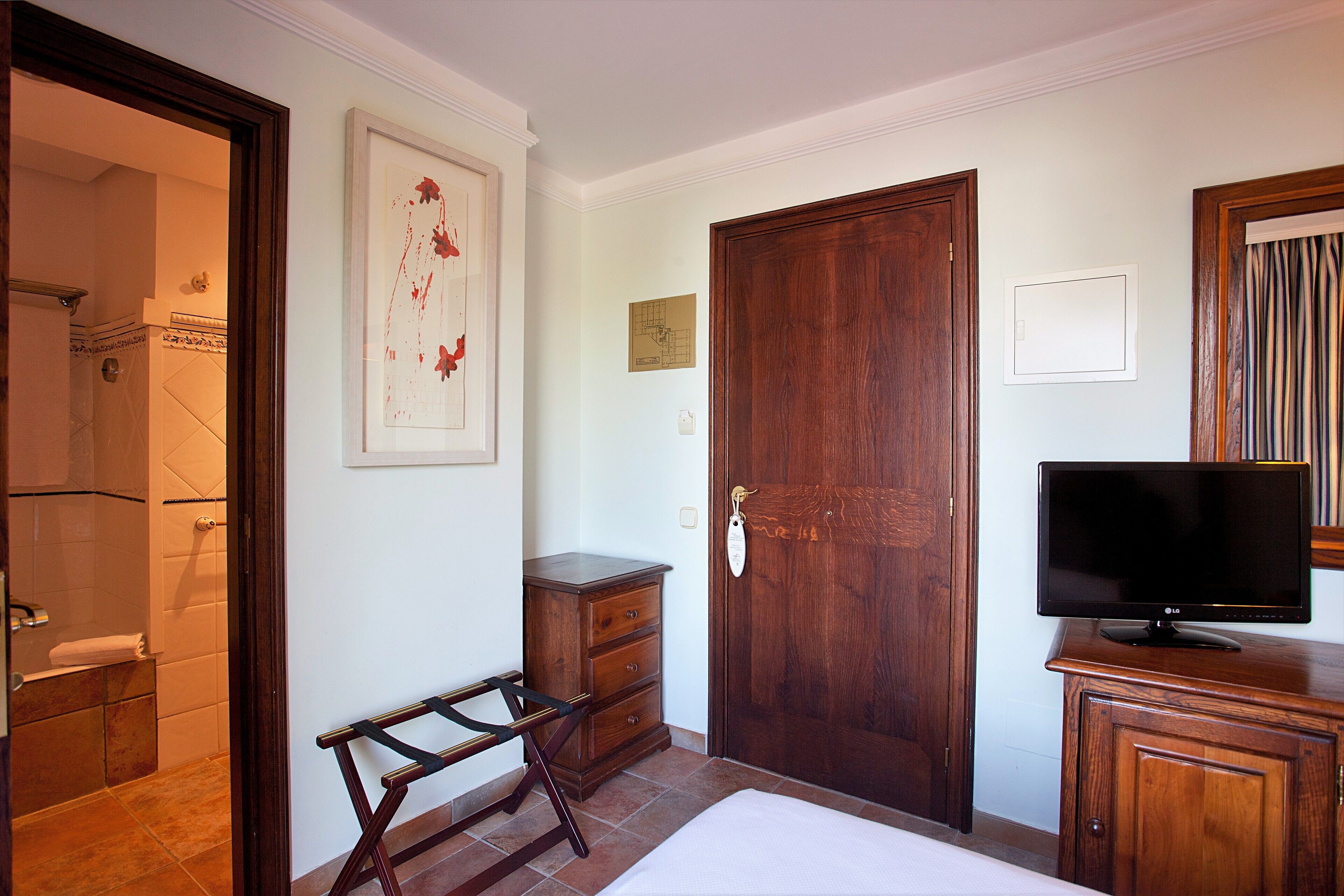 Quarto de hotel com chuveiro, cómoda de madeira, televisão e cama.