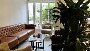 Uma sala de estar com um sofá de couro marrom, uma poltrona bege, uma mesa de centro de vidro e uma grande planta verde.