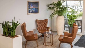Uma área de estar moderna com poltronas de couro, uma mesinha e uma planta grande em vaso.