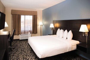 Quarto de hotel com uma cama grande, duas luminárias de cabeceira, uma televisão de tela plana, uma escrivaninha e uma janela com cortinas.