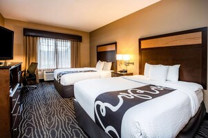 Quarto de hotel com duas camas, televisão, escrivaninha e uma cadeira.