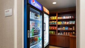 Uma área de despensa com um refrigerador Pepsi cheio de bebidas e lanches.