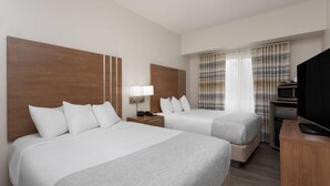Quarto de hotel com duas camas, uma escrivaninha, televisão e cortinas.