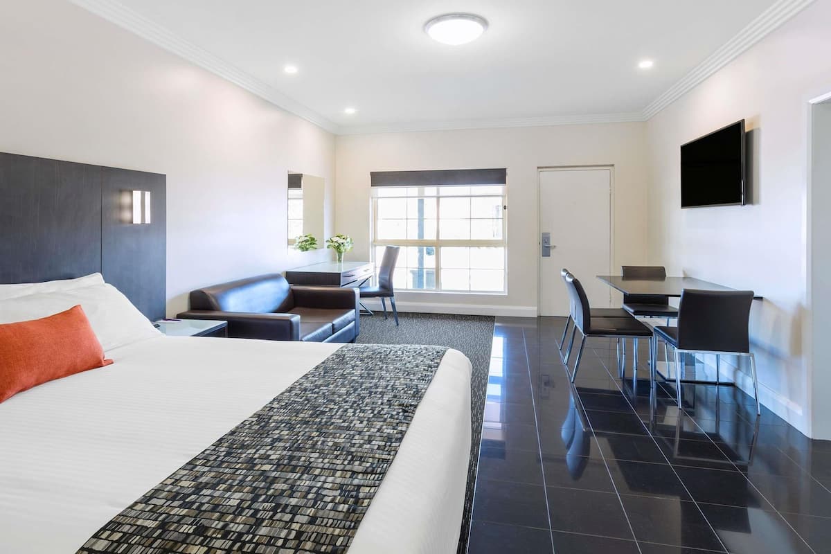 Quarto de hotel moderno com uma cama grande, uma escrivaninha, uma cadeira, uma TV e uma janela.