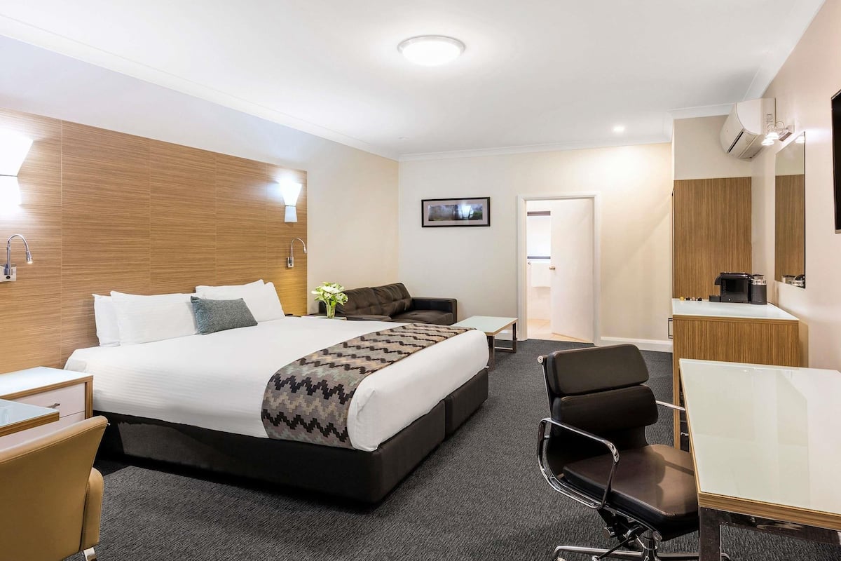 Quarto de hotel com cama, mesa de cabeceira, cadeira, escrivaninha e espelho.