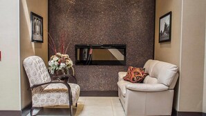 Um quarto com parede estampada, um sofá, uma poltrona e uma pequena mesa com um vaso de flores.