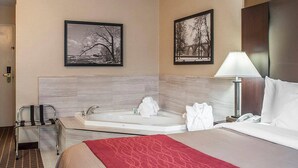 Quarto de hotel com cama, banheiro com banheira, uma cadeira e duas quadros na parede.