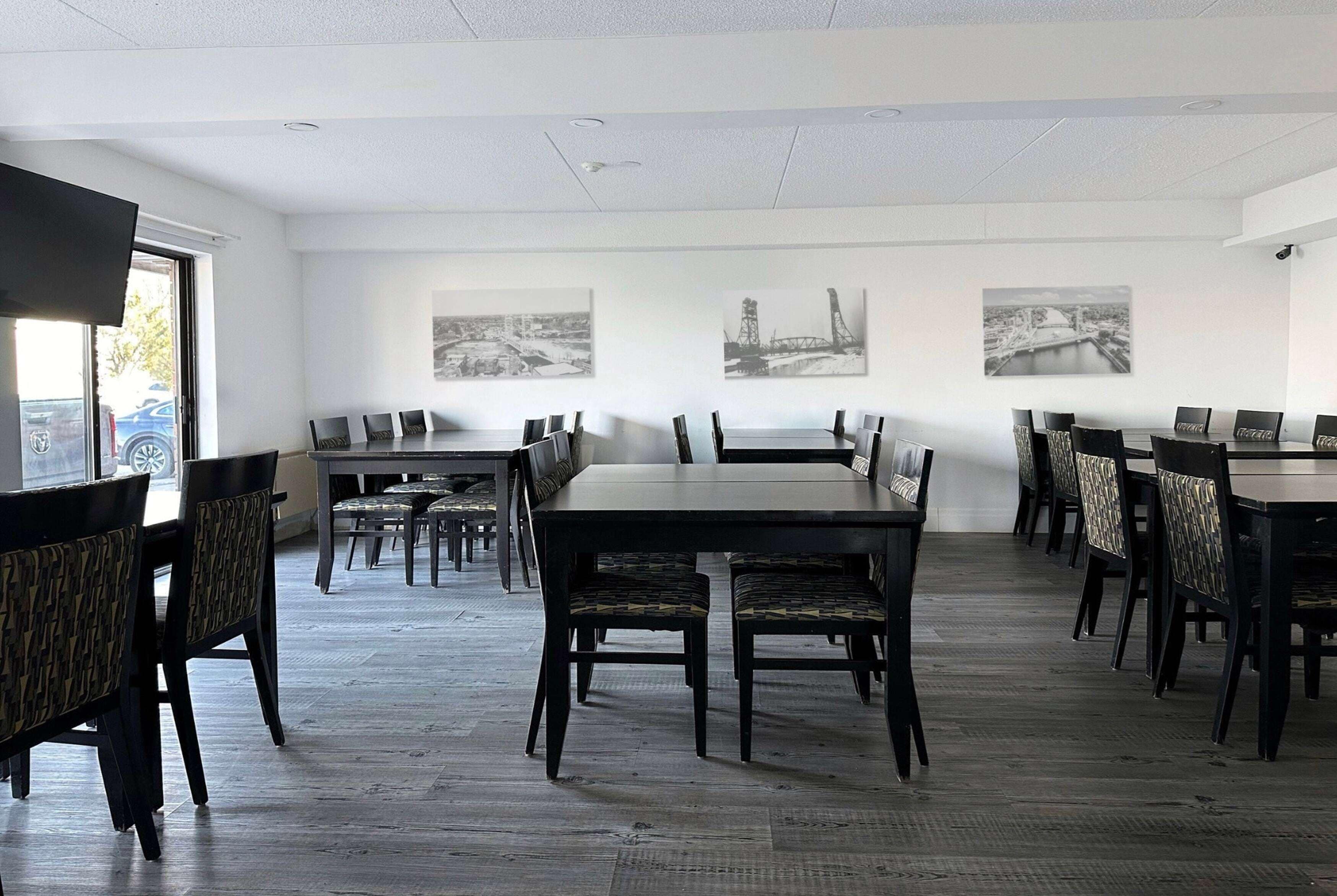 Uma sala de conferência com várias mesas e cadeiras, grandes janelas e fotografias preto e branco nas paredes.