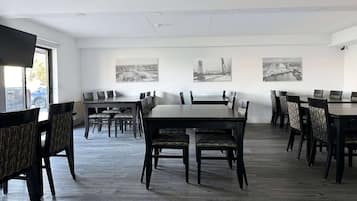 Uma sala de conferência com várias mesas e cadeiras, grandes janelas e fotografias preto e branco nas paredes.