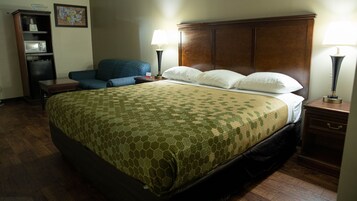 Quarto de hotel com cama grande, duas luminárias de cabeceira, cabeceira de madeira, poltrona azul, mesinha e um armário com micro-ondas.