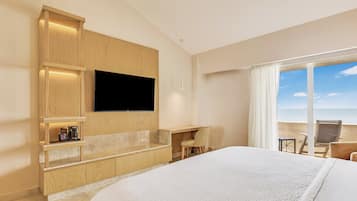 Quarto de hotel com uma cama grande, uma escrivaninha com cadeira, uma TV fixada na parede e uma varanda com vista para o mar.