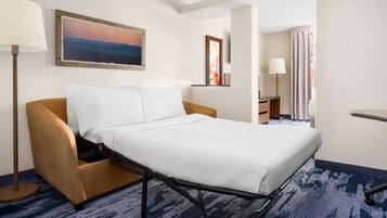 Quarto de hotel com cama, cadeira, escrivaninha e abajur.