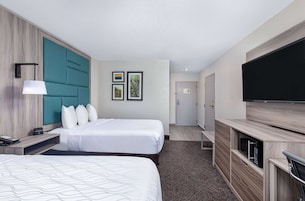 Quarto de hotel com duas camas, televisão, secretária com candeeiro e porta para a casa de banho.