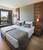 Quarto de hotel com duas camas, uma janela grande com vista para uma mesquita e uma mesa de cabeceira com abajur.