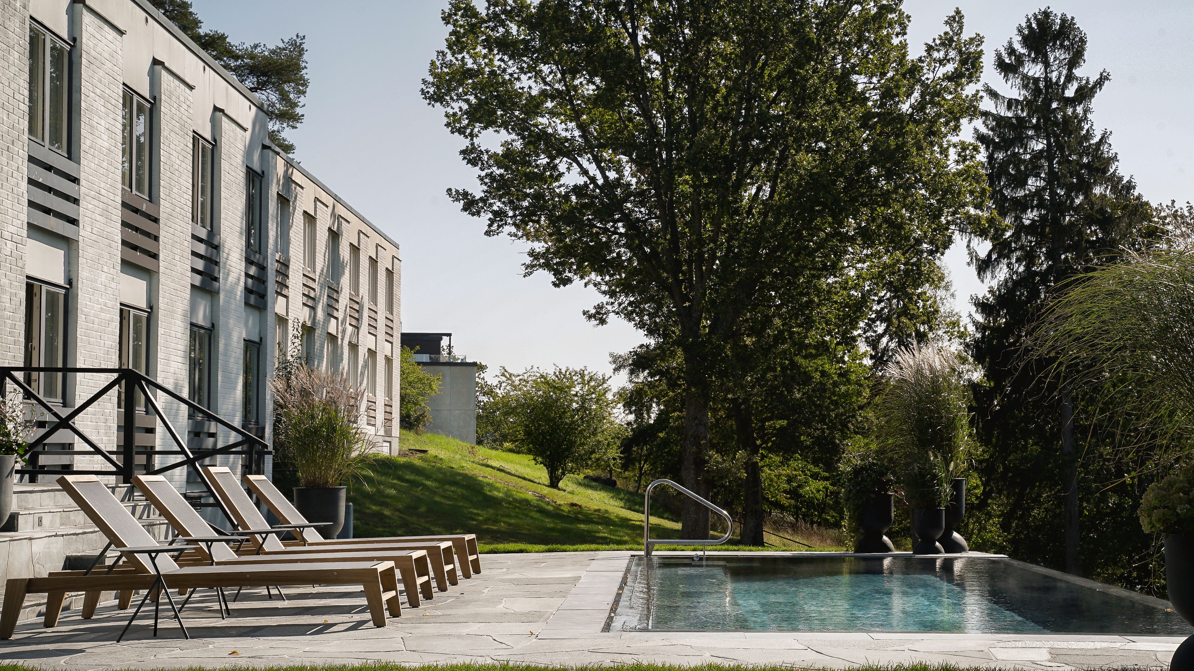Uma área de piscina com espreguiçadeiras, uma escadaria e um edifício com grandes janelas.