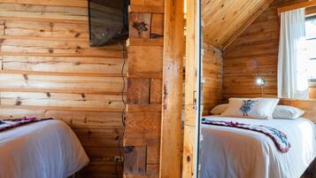 Quarto de cabana de madeira com duas camas, teto de madeira e janela com cortinas.