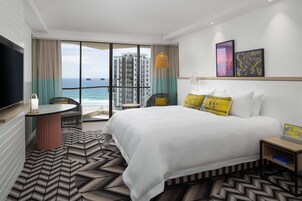 Quarto de hotel com uma cama grande, uma escrivaninha, uma cadeira e vista para o oceano.