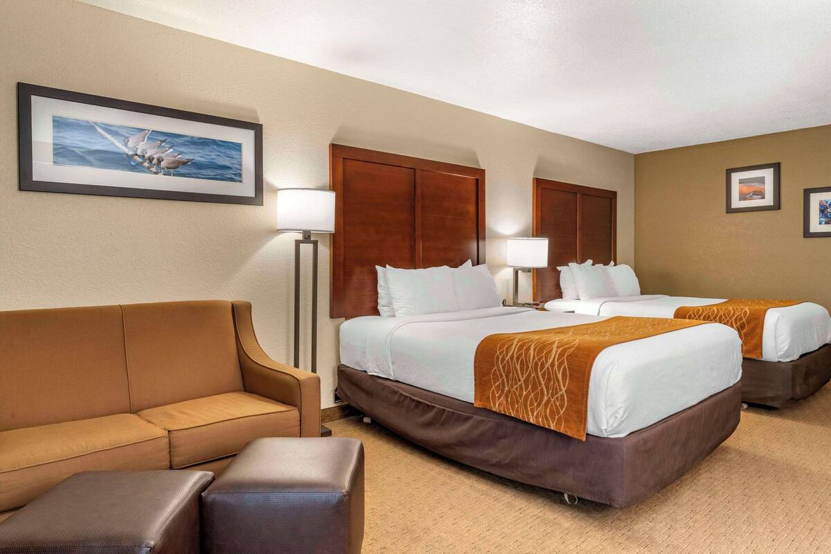 Quarto de hotel com duas camas, um sofá e um quadro pendurado na parede.