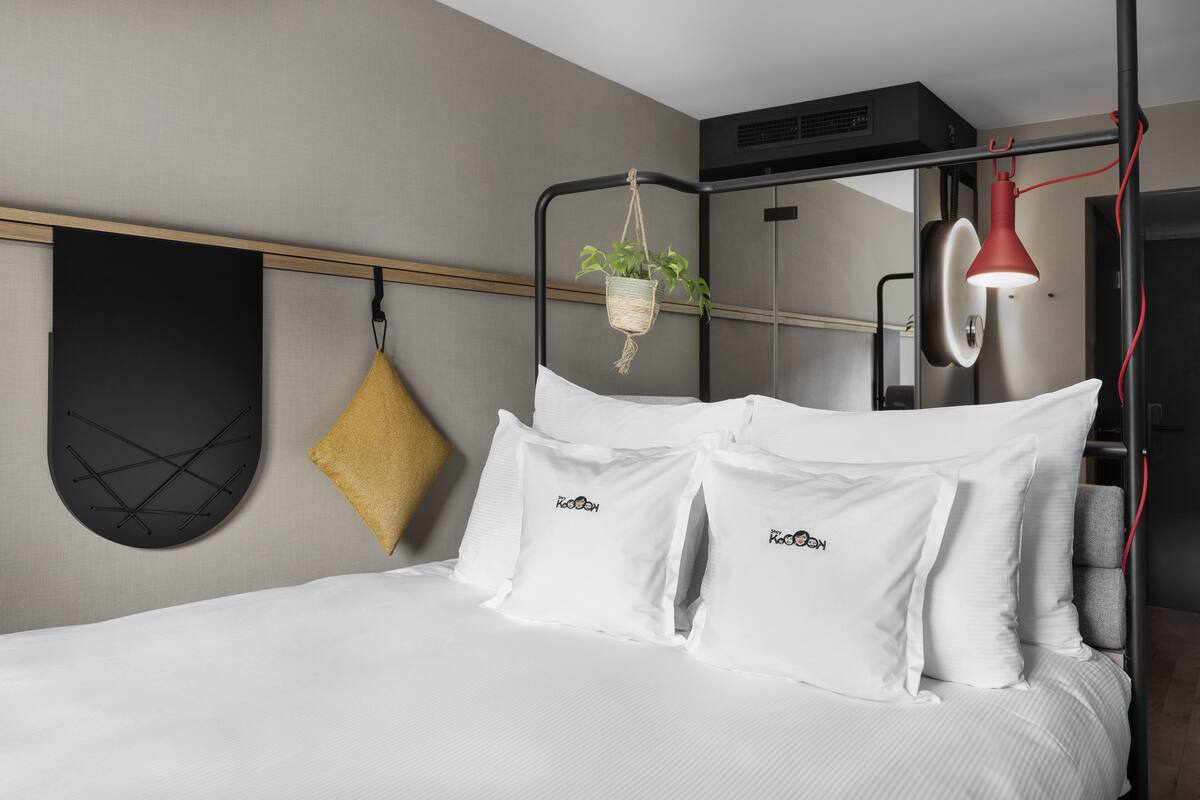 Quarto de hotel bem arrumado com uma cama beliche, uma planta pendente e uma luminária pendurada vermelha.
