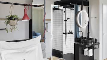 Quarto de hotel moderno com uma cama, planta pendente, luminária pendente vermelha, toucador preto com espelho e área de chuveiro.