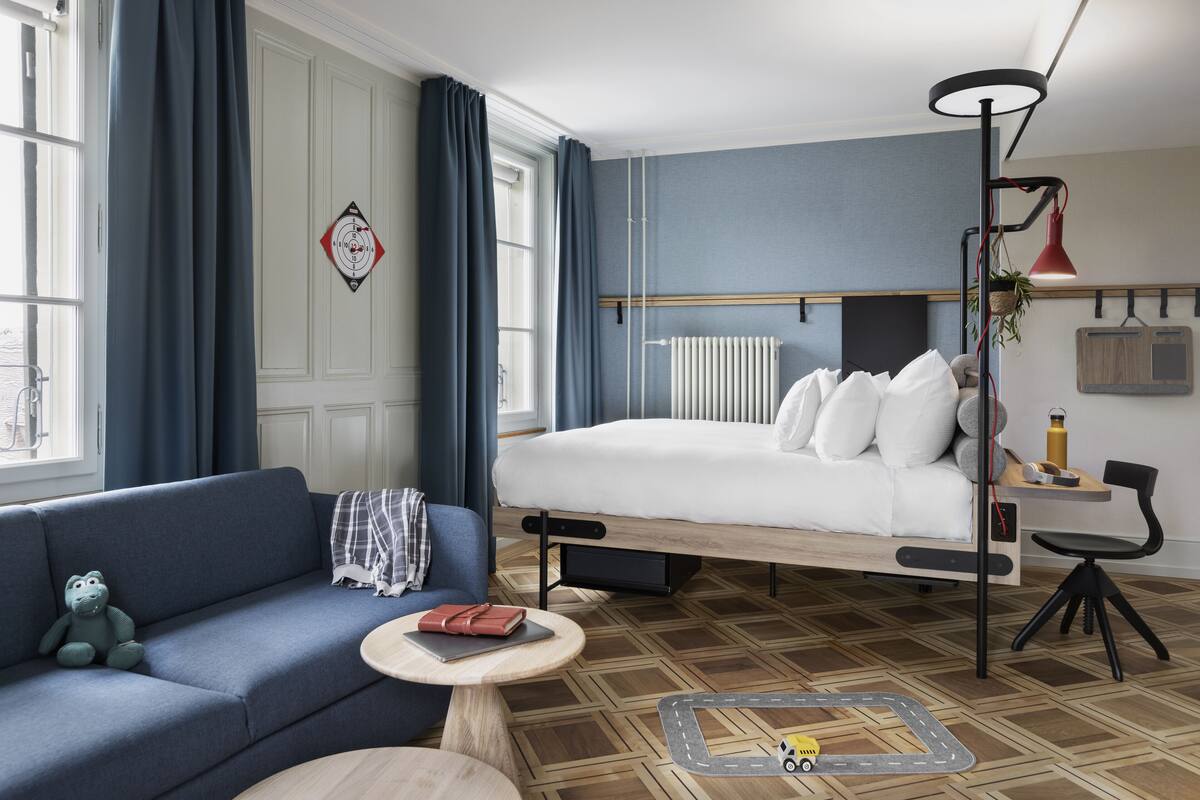 Quarto moderno com cama, sofá, mesa pequena e luminária de chão.