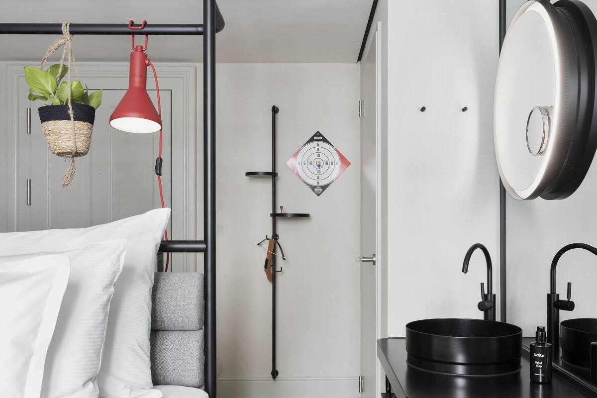 Quarto moderno com cama, mesa de cabeceira, luminária pendente vermelha e uma pequena planta.