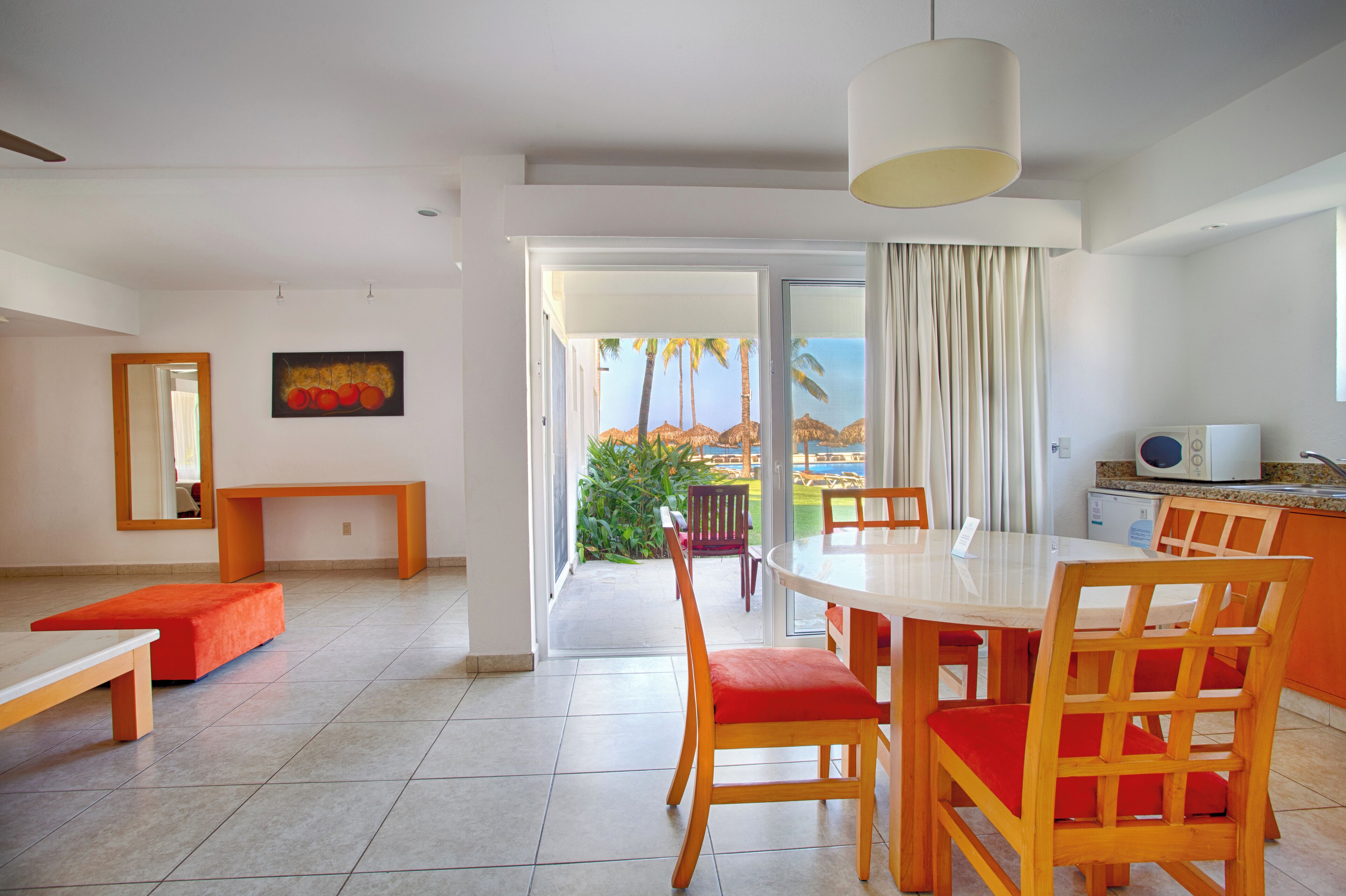 Quarto de hotel moderno com área de refeições, um banco, uma mesa e vista para palmeiras e montanhas.