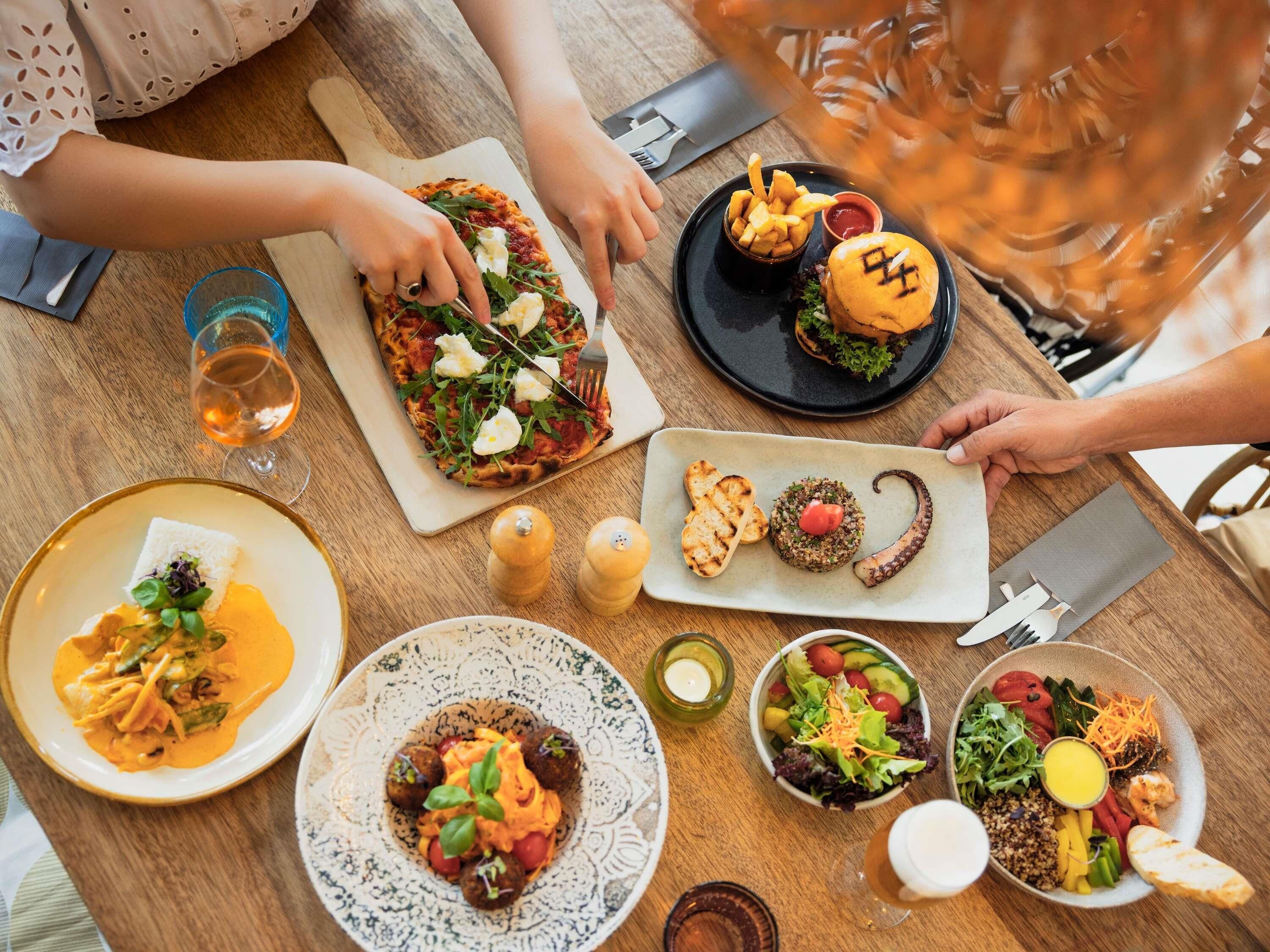 Uma mesa de jantar com diversos pratos, incluindo pizza, hambúrguer e salada.