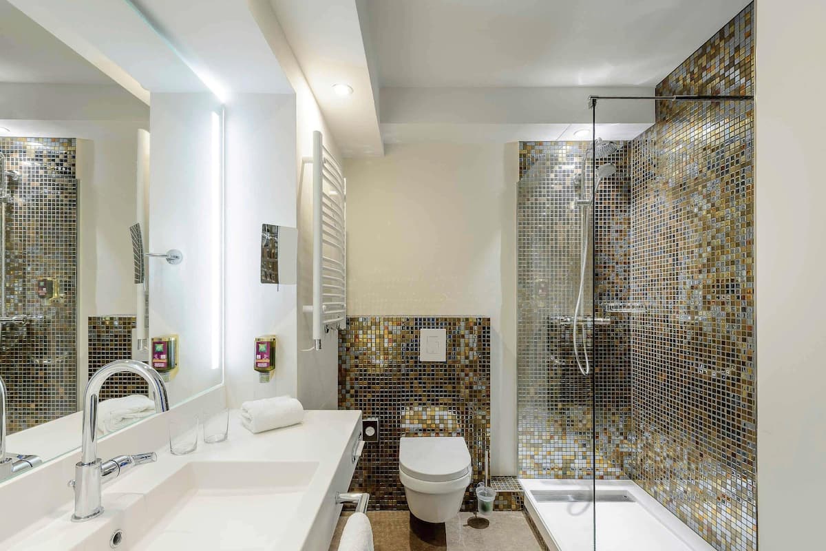 Uma casa de banho moderna com um espelho grande, uma sanita branca, uma pia e uma área de duche.