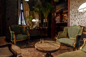 Um quarto luxuoso com poltronas estofadas verde com detalhes elaborados, uma mesa de centro de mármore e um tapete estampado.