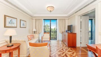 Quarto de hotel com sofá estampado, mesa de centro de madeira, televisão e vista para o exterior.