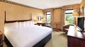 Quarto de hotel com uma cama grande, uma mesa com cadeira, uma televisão e uma janela com cortinas.