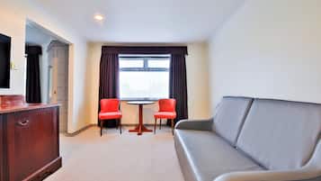 Quarto de hotel com um sofá cinzento, duas cadeiras vermelhas, um armário de madeira e uma pequena mesa redonda.