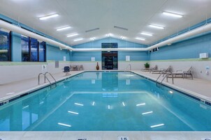 Uma grande piscina interna com água cristalina, rodeada por espreguiçadeiras e uma cadeira de salva-vidas, com esquema de cores azul e branco e uma placa indicando as regras da piscina.