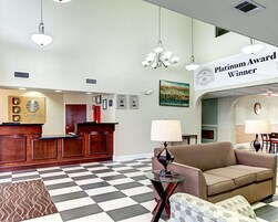 Um hall de hotel com piso xadrez, balcão de recepção, sofá e lustre.