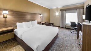 Quarto de hotel com uma cama grande, mesas de cabeceira, uma escrivaninha com cadeira, televisão e uma janela com cortinas.