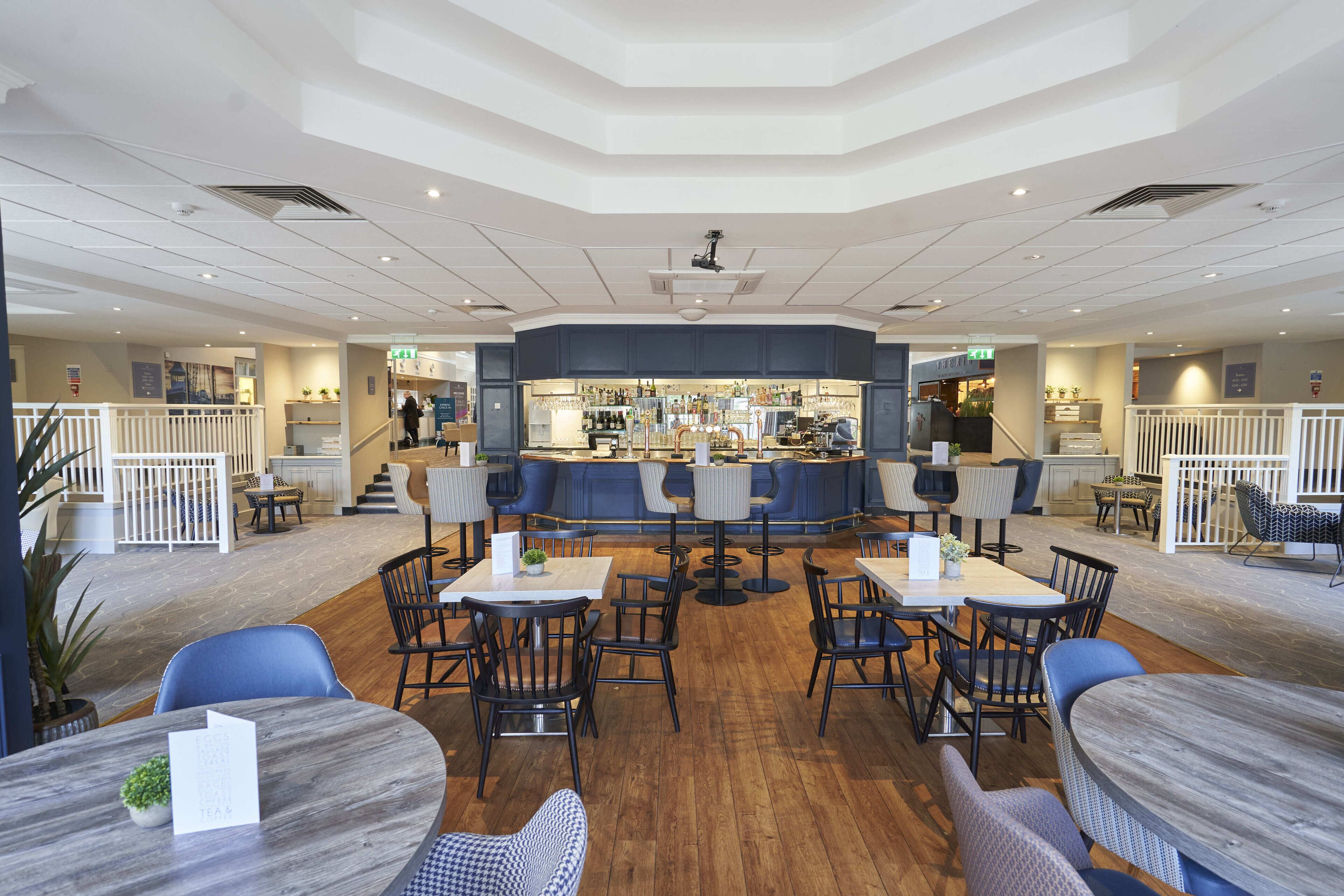 Um restaurante moderno com um bar central, diversas áreas de estar e piso de madeira.