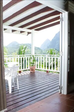 Uma área externa coberta com deck de madeira, guarda-corpo branco e um vaso com planta.