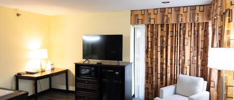 Quarto de hotel com televisão de tela plana, uma escrivaninha com luminária, uma cadeira e cortinas estampadas.