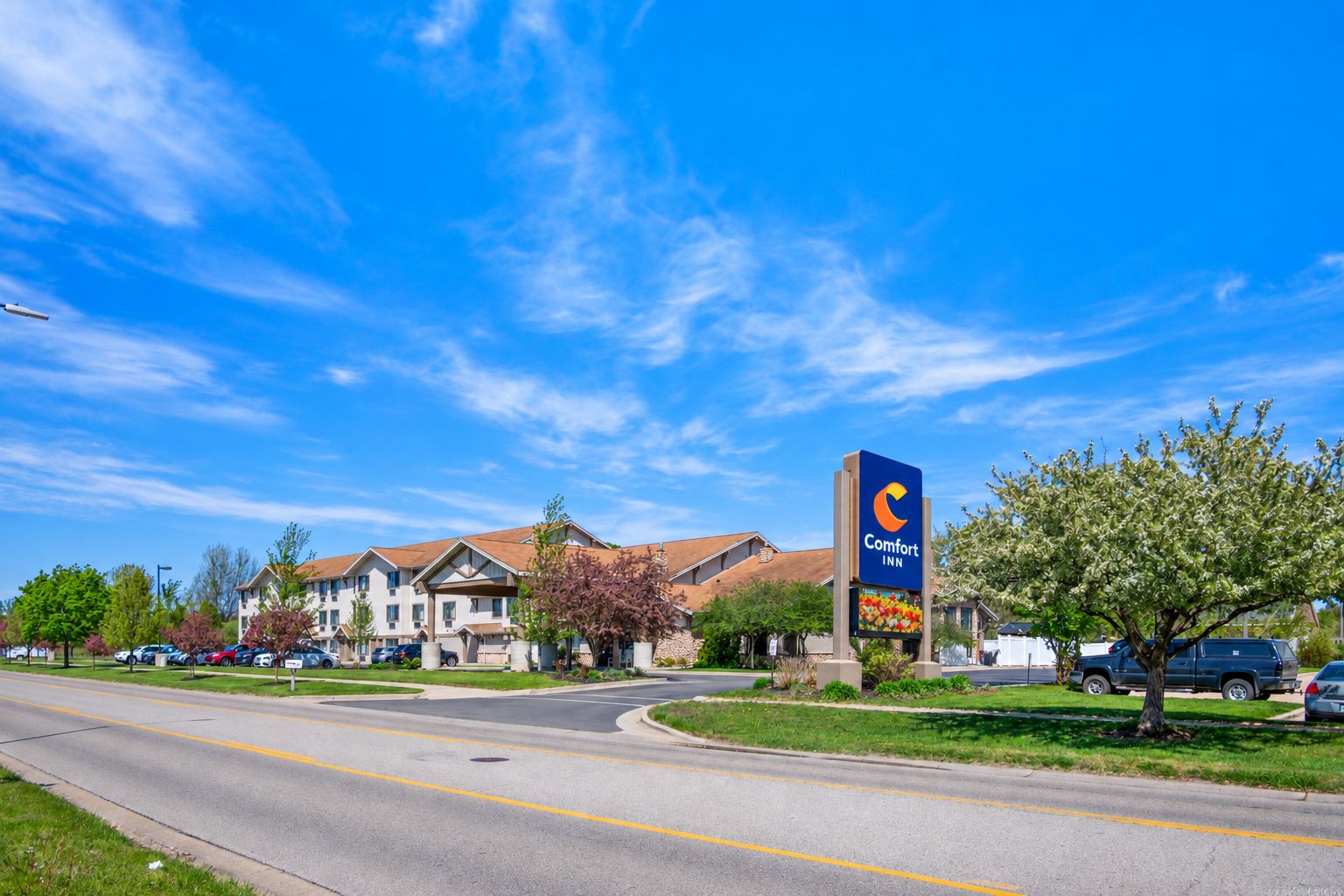 Um hotel Comfort Inn com céu azul claro, estacionamento com carros e estrada com faixa amarela.