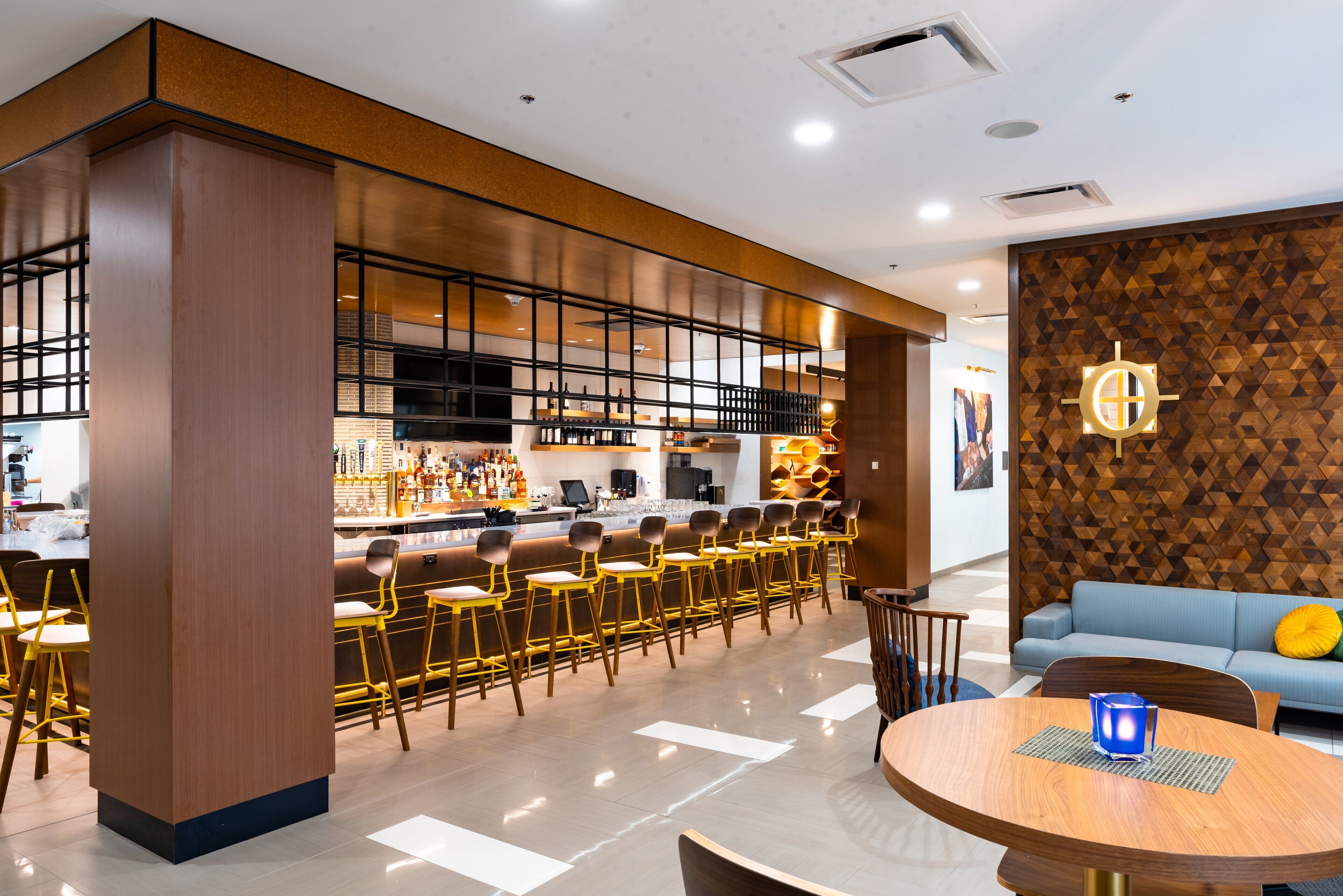 Uma área de bar moderna com um balcão comprido, vários banquetes e um espaço de estar com uma mesa redonda e cadeiras.