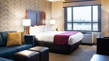 Quarto de hotel com cama, sofá, escrivaninha e uma grande janela com vista para a cidade.