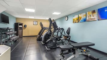 Uma academia com equipamentos de ginástica, um relógio e pôsteres motivacionais na parede.
