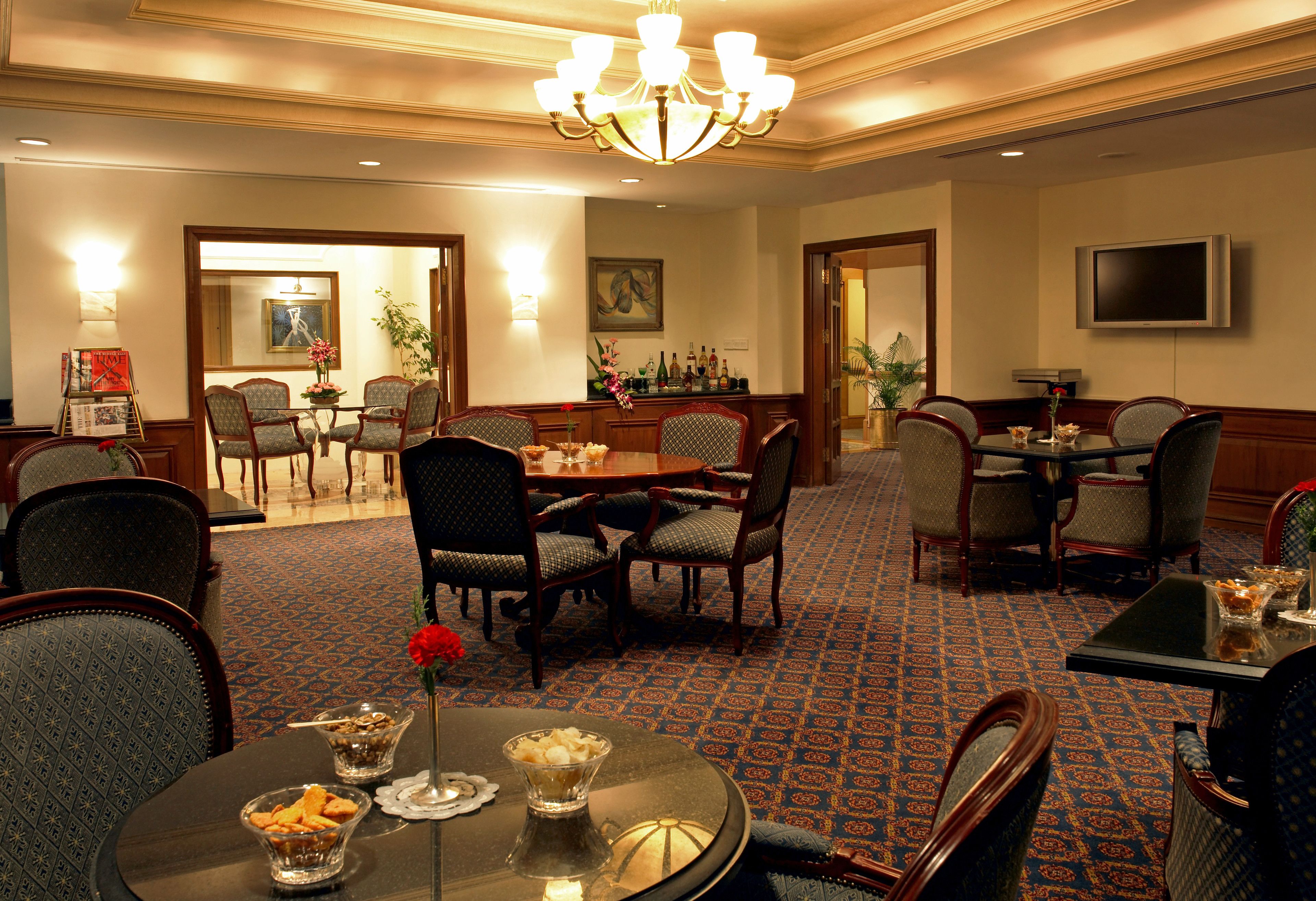 Uma sala de jantar de hotel com um candelabro, várias mesas e cadeiras.