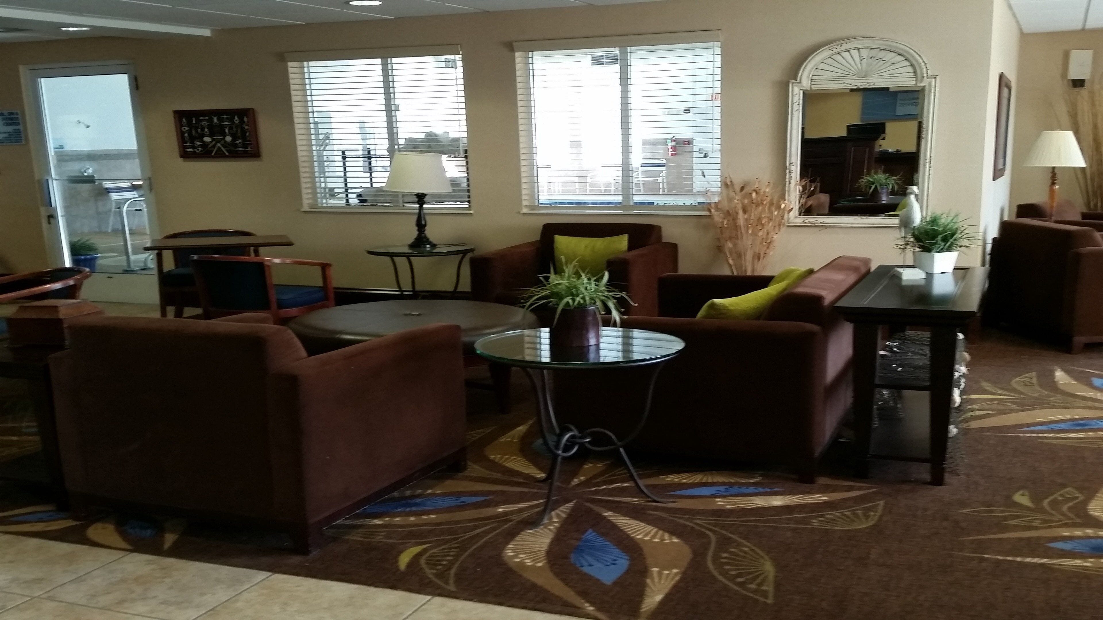 Um hall de hotel com uma mesa de vidro redonda, sofás marrons, uma planta em vaso e um espelho.