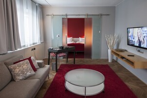 Uma sala de estar moderna com sofá, parede de destaque vermelha, televisão e área de jantar.