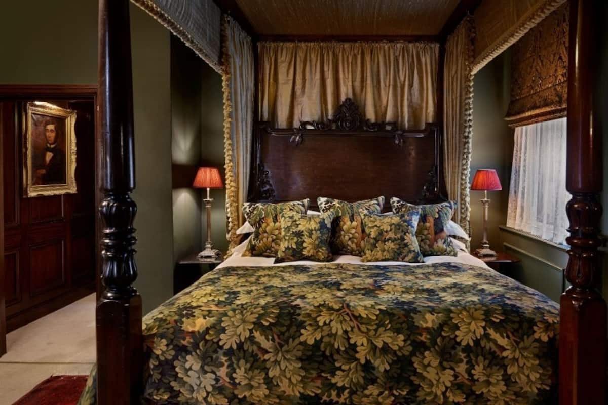 Uma cama com dossel com colcha floral, duas luminárias de cabeceira e um retrato emoldurado na parede.