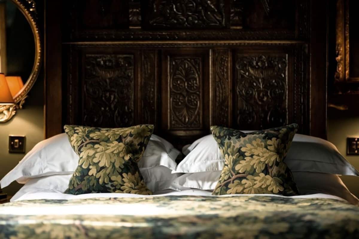 Cama com almofadas estampadas em floral e cabeceira de madeira com esculturas detalhadas.