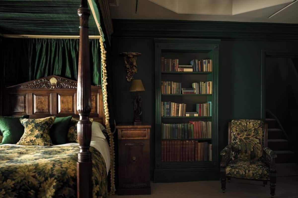Quarto com cama de dossel, estante, cadeira e abajur.